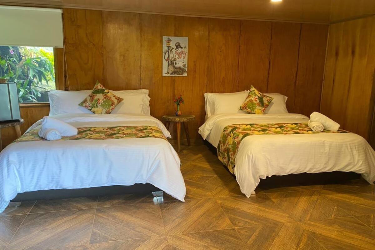 Quarto com duas camas, paredes de madeira, uma mesa redonda pequena e um quadro na parede.