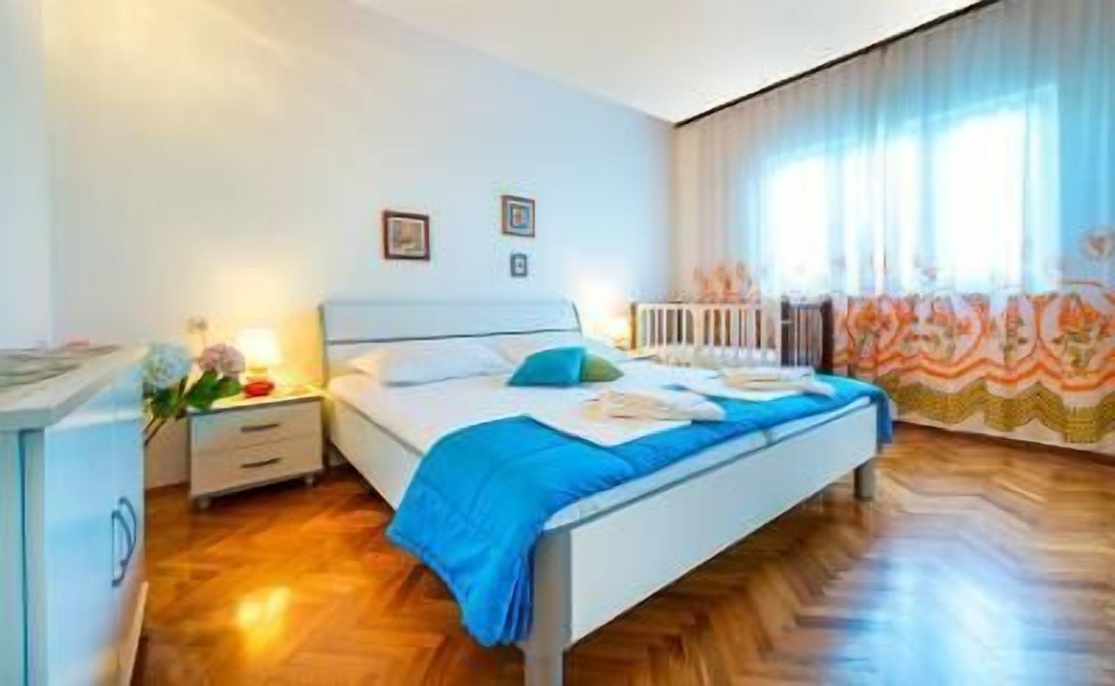 Quarto com cama, mesa de cabeceira, cômoda e janela com cortinas.