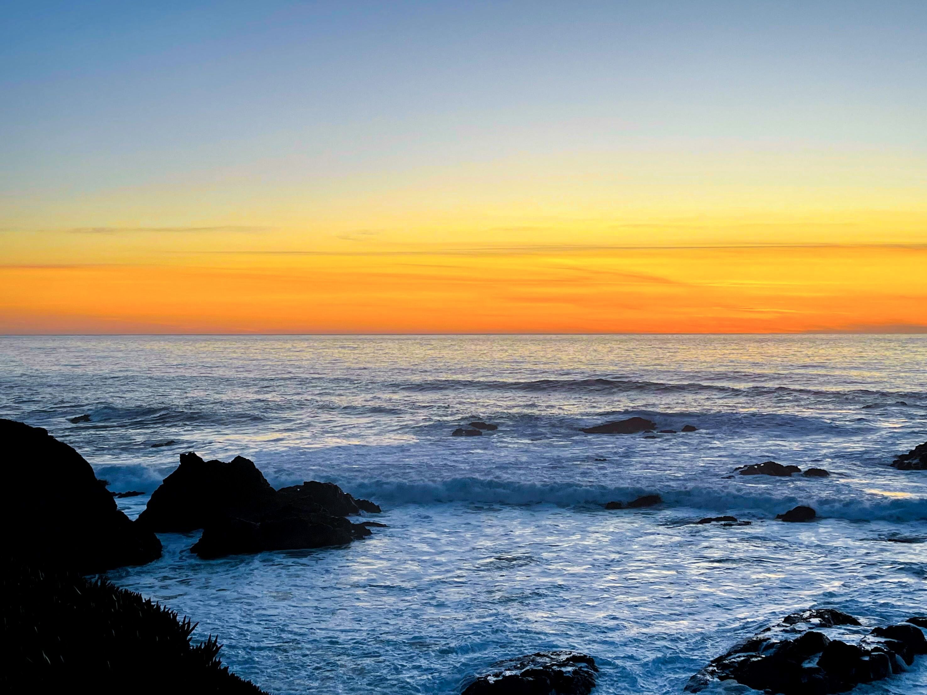 Um pôr do sol costeiro com ondas quebrando nas rochas.