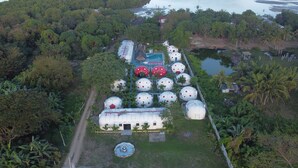 Vista aérea de um resort com acomodações esféricas e em forma de cúpula, piscina e um pequeno lago.