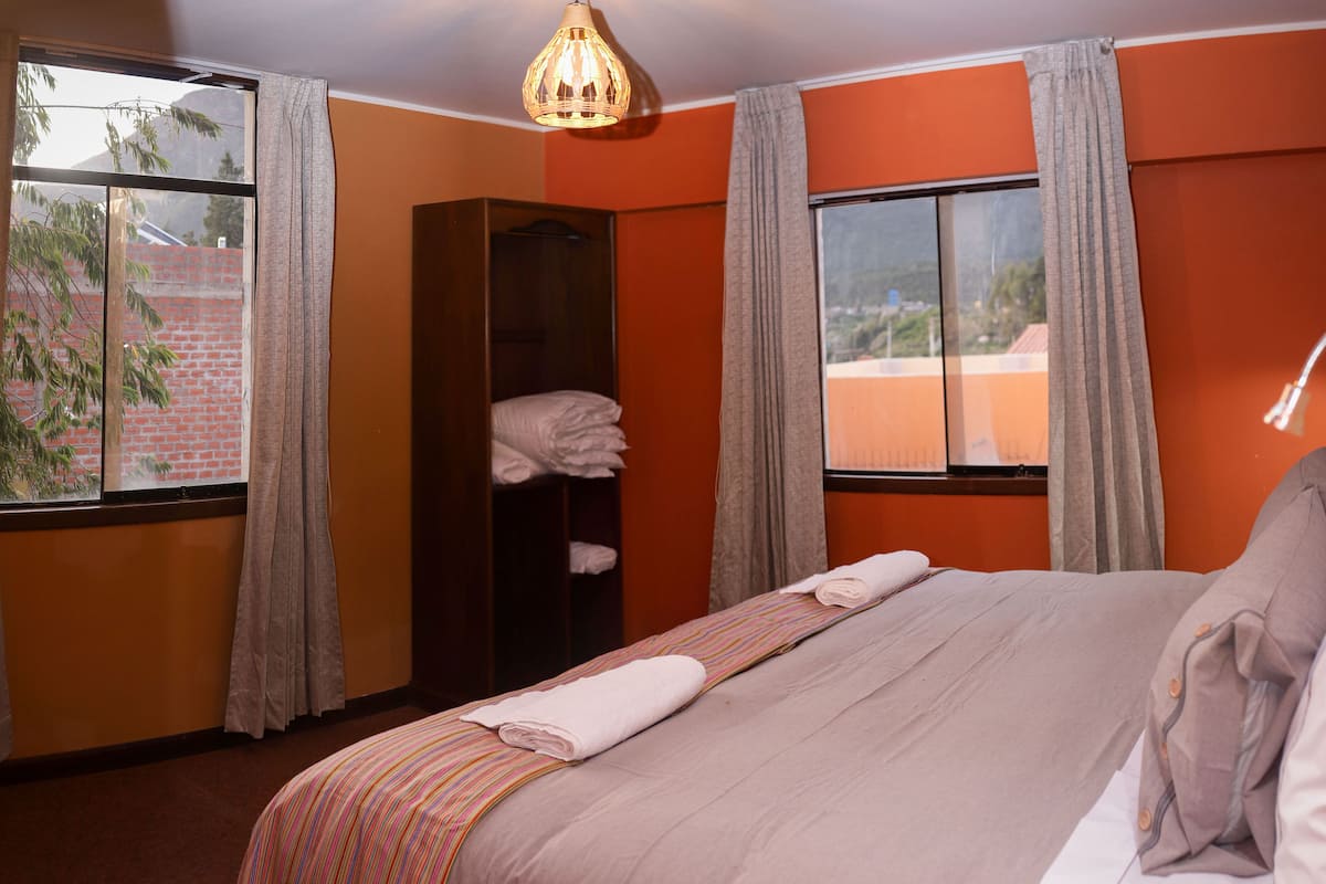 Quarto de hotel com uma cama, um guarda-roupa e duas janelas com cortinas.