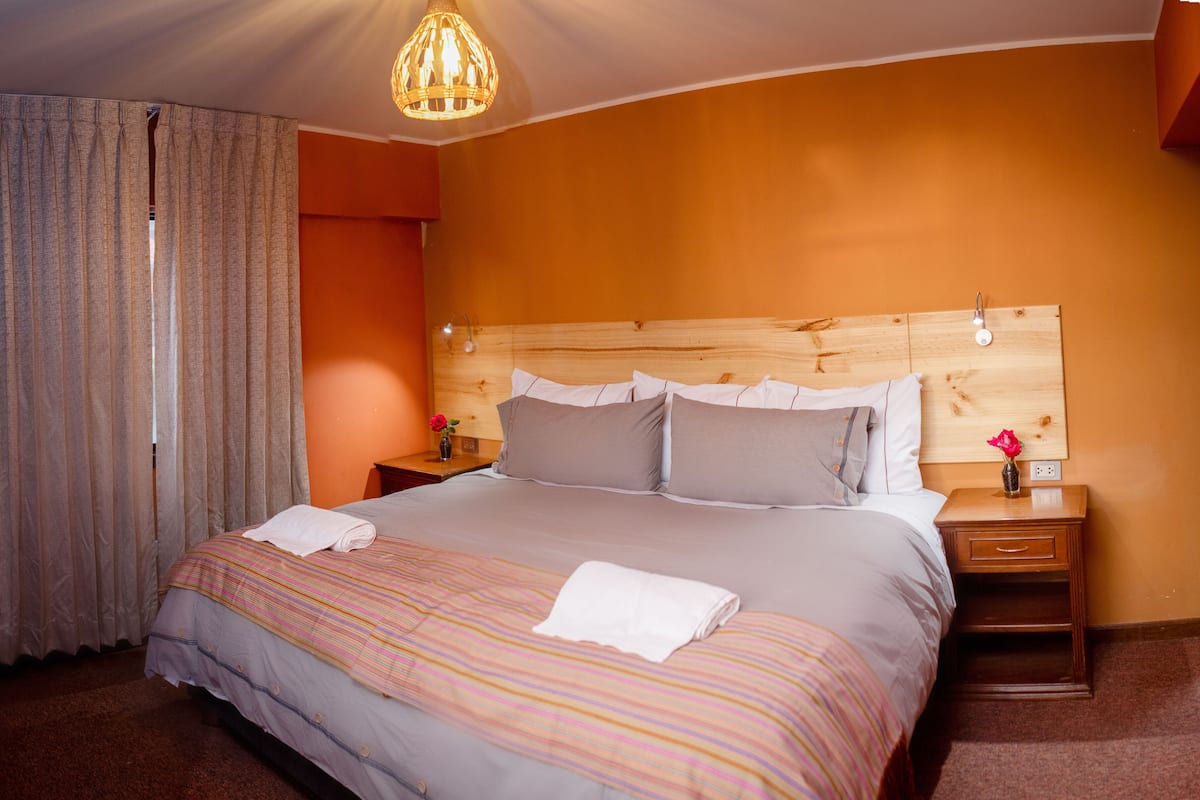 Quarto de hotel com uma cama grande, cabeceira de madeira e mesa de cabeceira com um vaso de flores.
