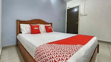 Quarto de hotel com cama, colcha estampada em vermelho e branco, e cabeceira de madeira.