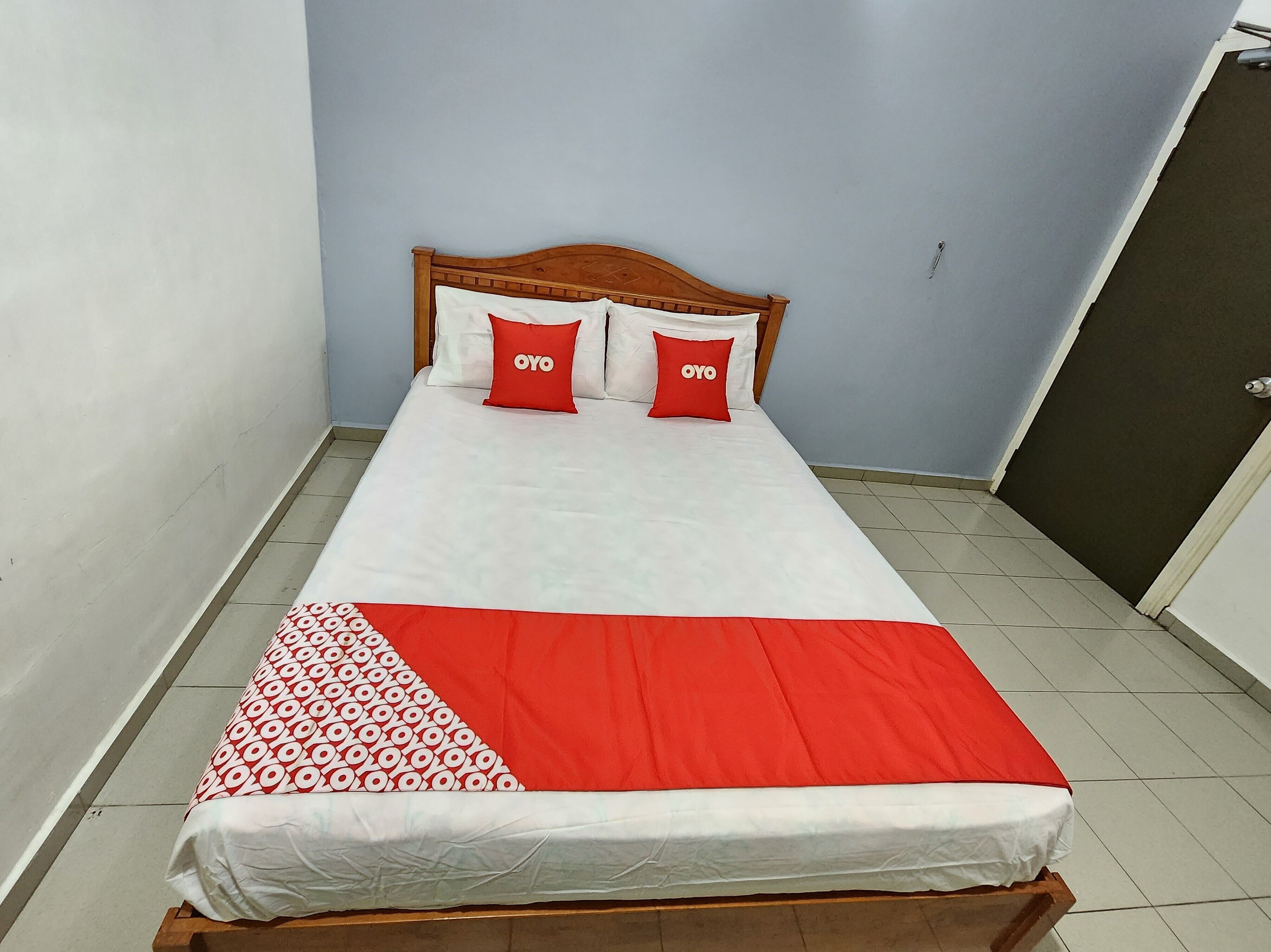 Quarto de casal com uma cama de solteiro, cabeceira de madeira, roupa de cama branca e duas almofadas vermelhas com a palavra "OYO".