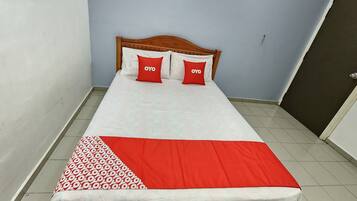 Quarto de casal com uma cama de solteiro, cabeceira de madeira, roupa de cama branca e duas almofadas vermelhas com a palavra "OYO".