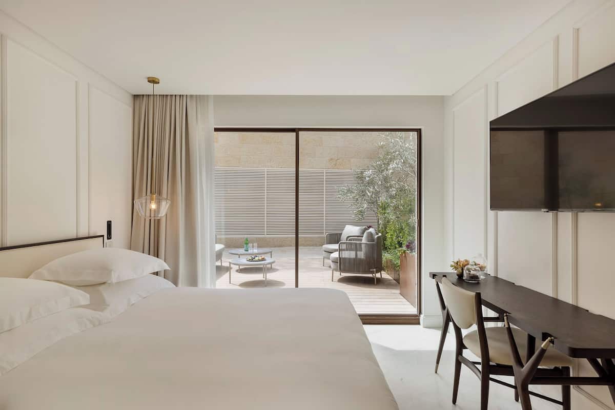 Quarto de hotel moderno com uma cama grande, uma mesa de jantar e uma varanda com área de estar ao ar livre.