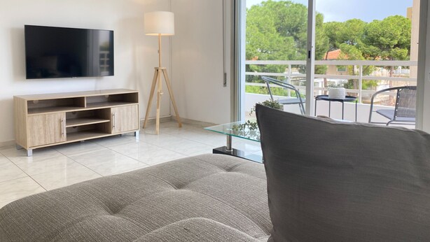 Uma sala de estar moderna com televisão de tela plana, mesa de centro de vidro, sofá cinza e abajur.