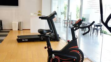 Uma academia com equipamentos de ginástica, incluindo uma bicicleta ergométrica e esteira, com amplas janelas e vista para o exterior.