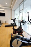 Uma academia com equipamentos de ginástica, incluindo uma bicicleta ergométrica e esteira, com amplas janelas e vista para o exterior.