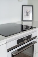 Cozinha com fogão por indução preto, forno de aço inoxidável e um quadro de um abacate na parede.