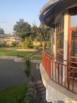 Um edifício moderno com varanda curva, paredes de pedra e um jardim bem cuidado, com diversas plantas e um caminho.