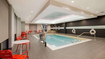 Área de piscina com cadeiras e mesas vermelhas, um posto de salva-vidas e uma parede escura com um detalhe decorativo branco.