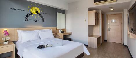 Quarto de hotel com cama, mesas de cabeceira, escrivaninha e parede com frase motivacional.