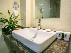 Um banheiro com pia branca, espelho, secador de cabelo e duas lixeiras.