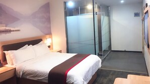 Quarto de hotel com cama, mesa de cabeceira, luminária e parede divisória de vidro.