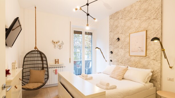 Quarto moderno com cama, cadeira suspensa, escrivaninha e televisão.