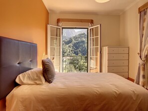 Quarto com cama grande, penteadeira e varanda com vista para a montanha.