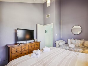 Um quarto com uma cama, uma televisão sobre um aparador de madeira, uma mesa de cabeceira, um espelho e uma porta.