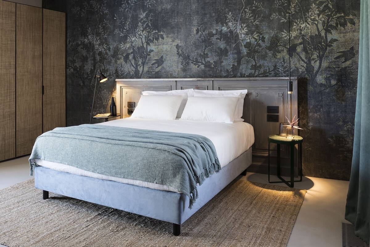 Quarto moderno com uma cama grande, parede texturizada escura e um guarda-roupa de madeira.