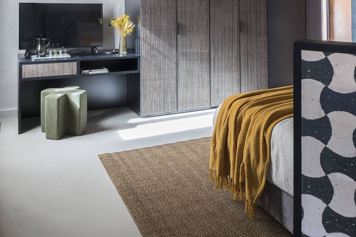 Quarto moderno com guarda-roupa espaçoso, televisão e cama com cabeceira estampada.