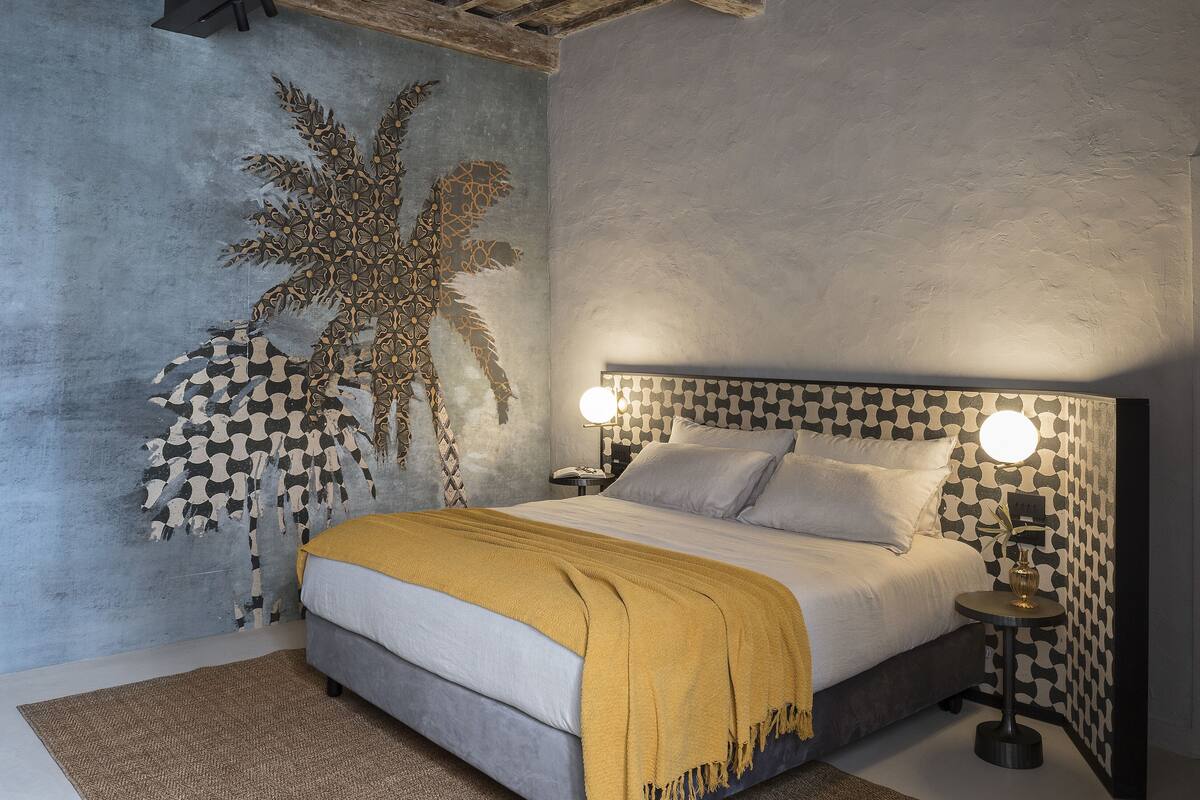 Quarto com cama, mesa de cabeceira, abajur e um mural na parede.