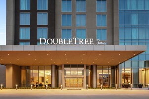 Entrada de hotel com fachada moderna, janelas amplas e uma placa com a inscrição 'DOUBLETREE by Hilton'.