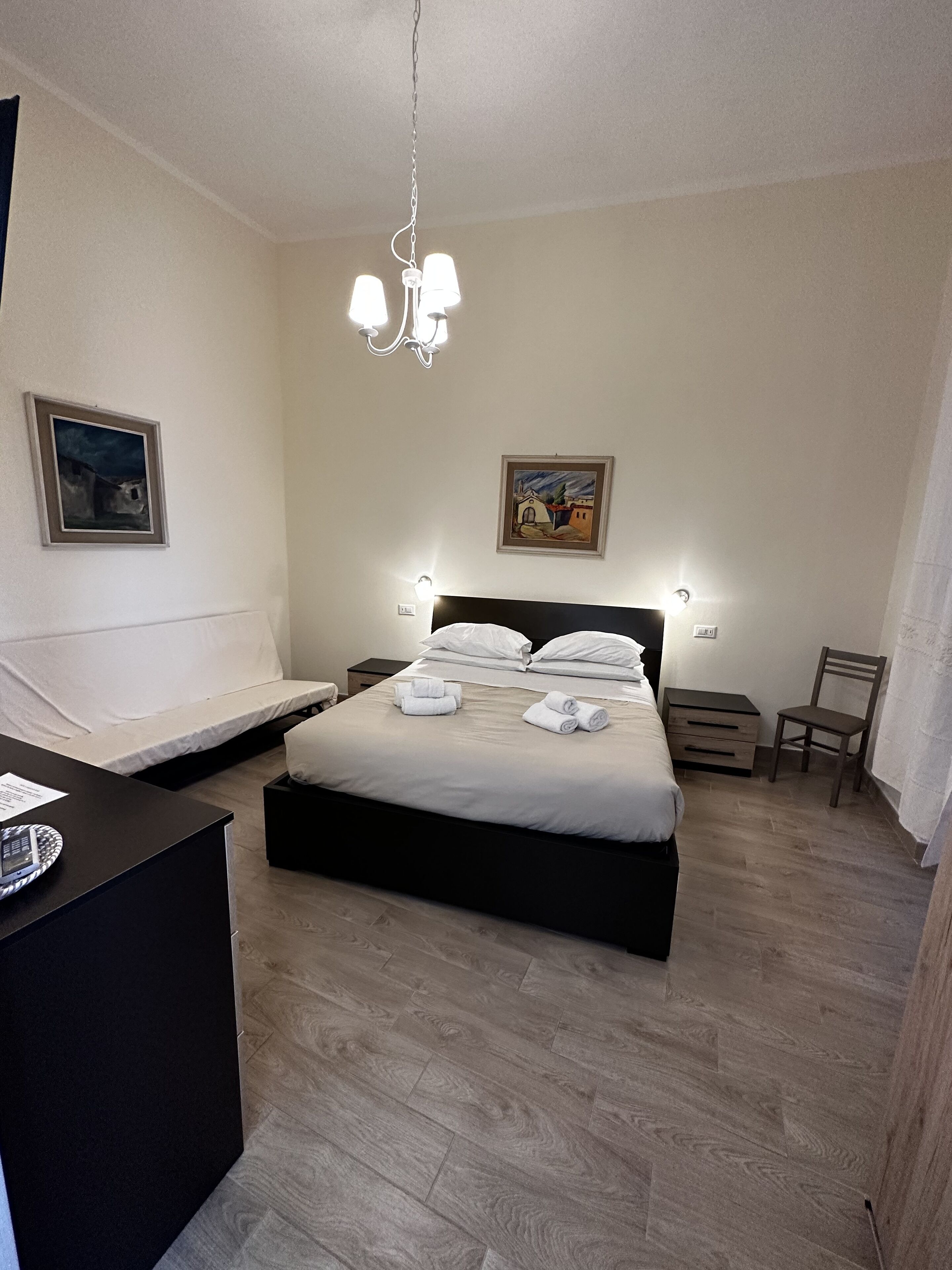 Quarto bem arrumado com uma cama, mesas de cabeceira, escrivaninha e uma cadeira.