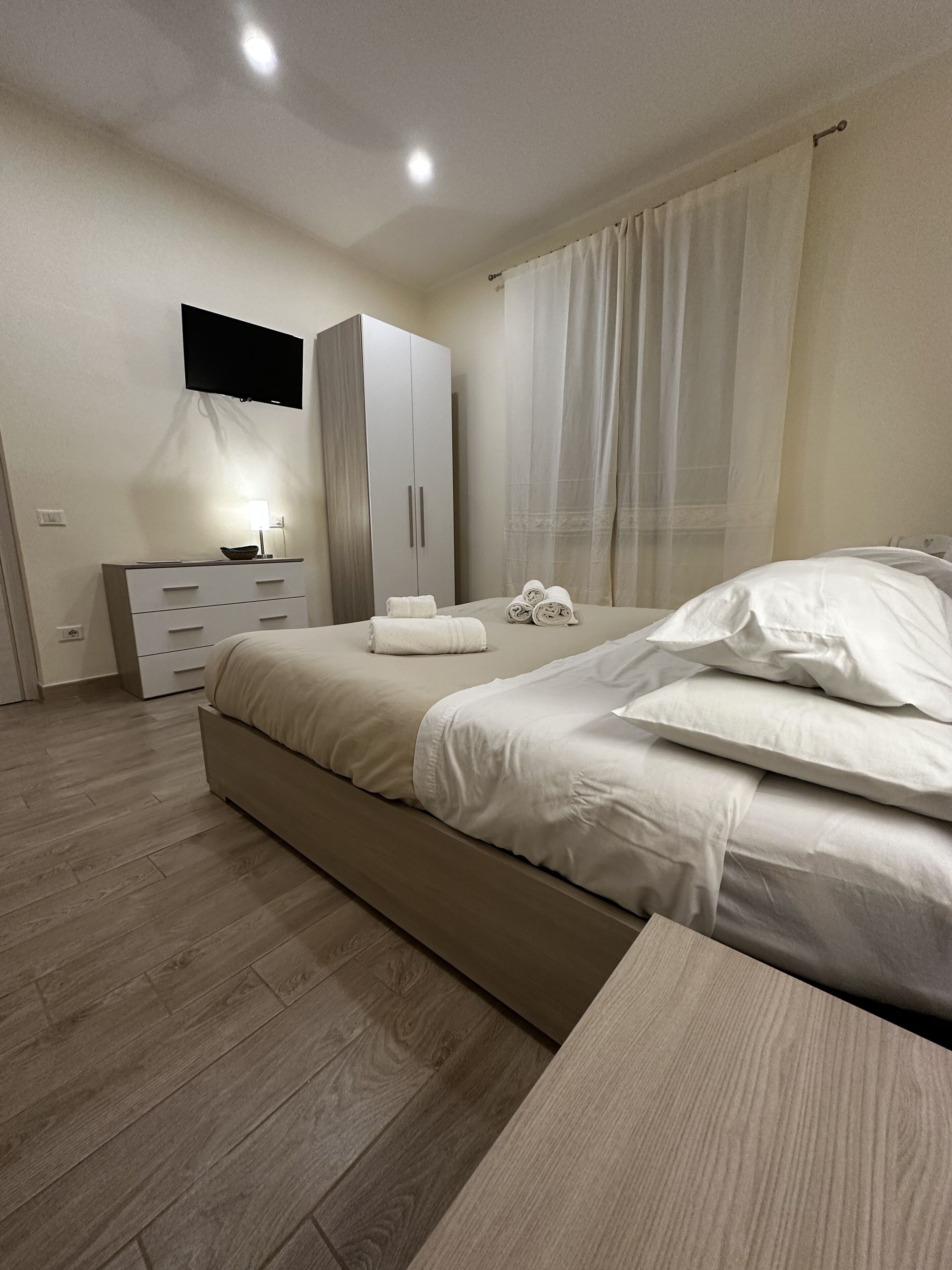 Quarto moderno com uma cama grande, um guarda-roupa, uma mesa de cabeceira e uma televisão de ecrã plano fixada na parede.