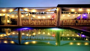 Um espaço para eventos ao ar livre com uma piscina refletora, tecido branco esvoaçante e luzes de corda.