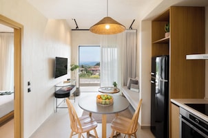 Uma cozinha moderna com uma geladeira preta, uma área de jantar com mesa e cadeiras redondas, e vista para o exterior por uma grande janela.