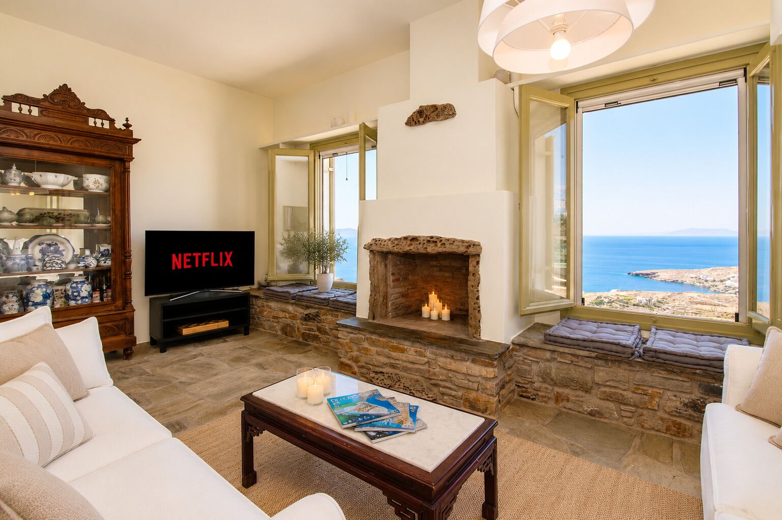 Uma sala de estar com lareira de pedra, televisão e vista para o mar.