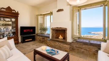 Uma sala de estar com lareira de pedra, televisão e vista para o mar.