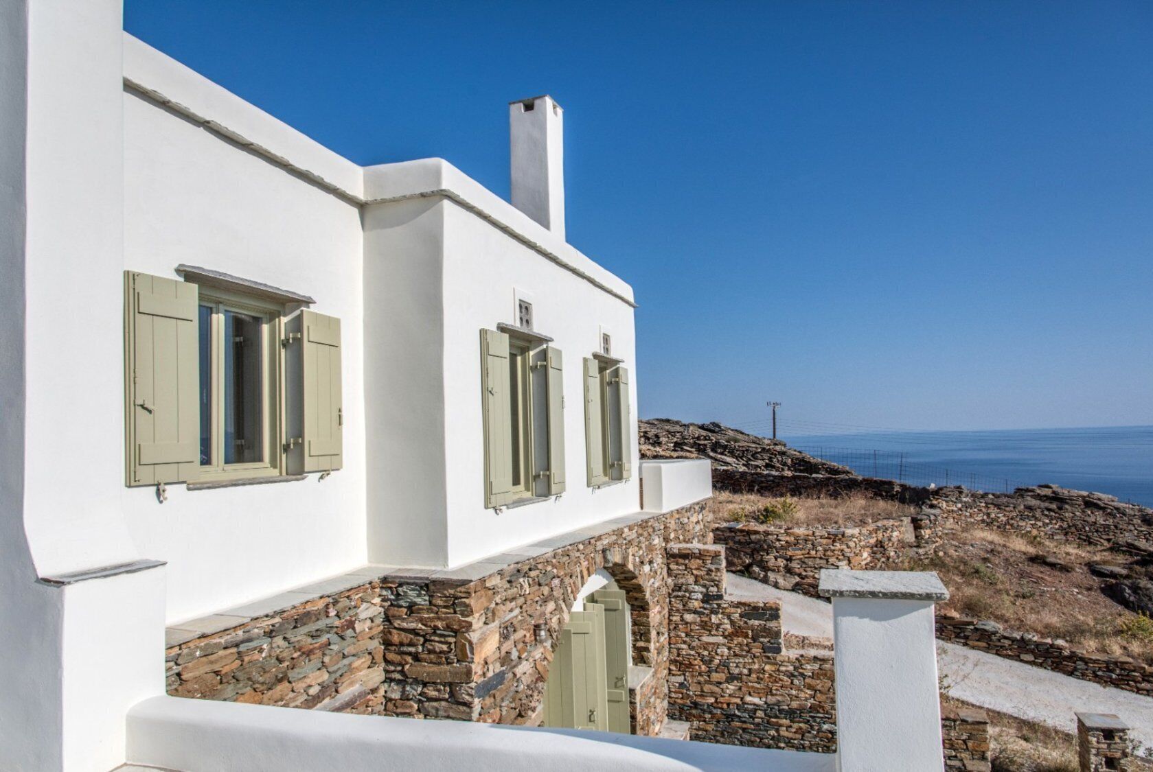 Um edifício branco com contraventanas verdes e degraus de pedra que levam a uma área rochosa.
