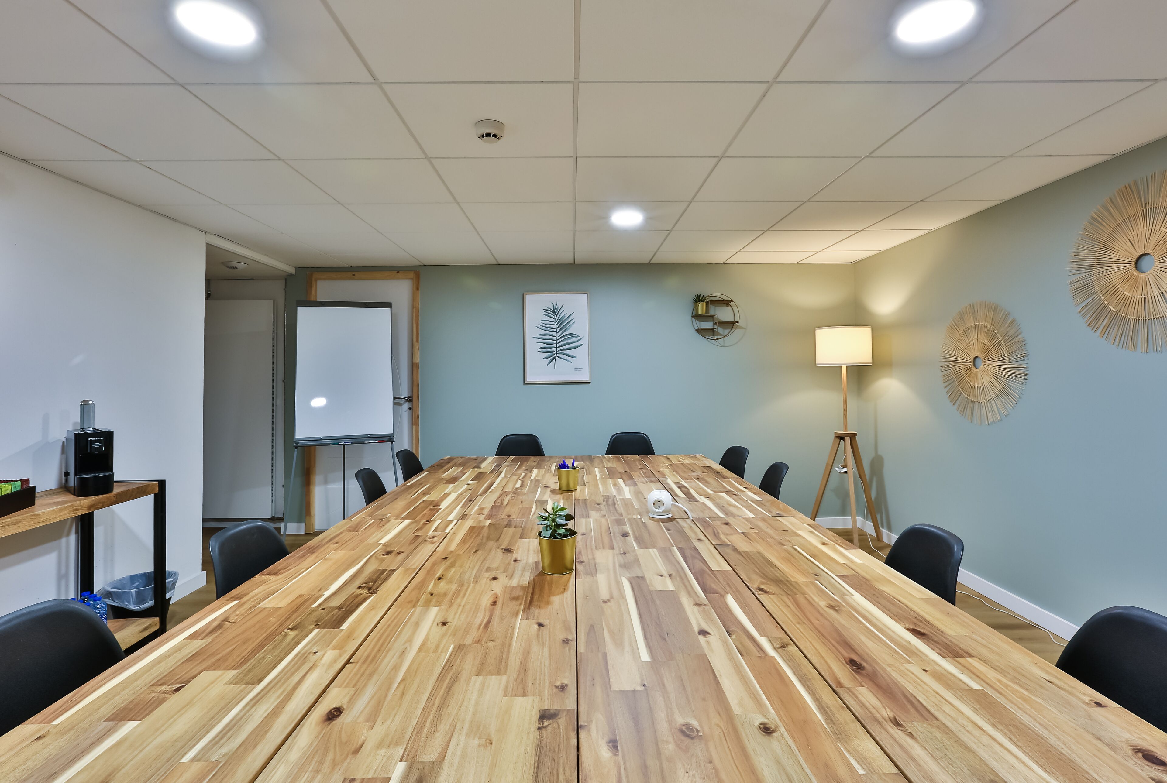 Sala de conferência com uma longa mesa de madeira, cadeiras pretas, um quadro branco e decoração na parede.