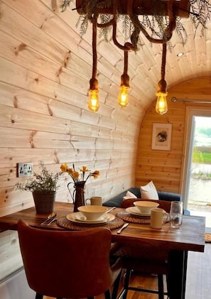 Interior em madeira com mesa de jantar posta para dois, luminária pendente e vista para o exterior.