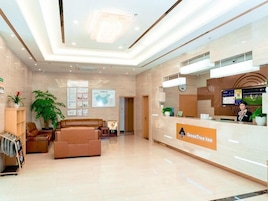 Um lobby de hotel com balcão de recepção, área de estar e uma grande planta.