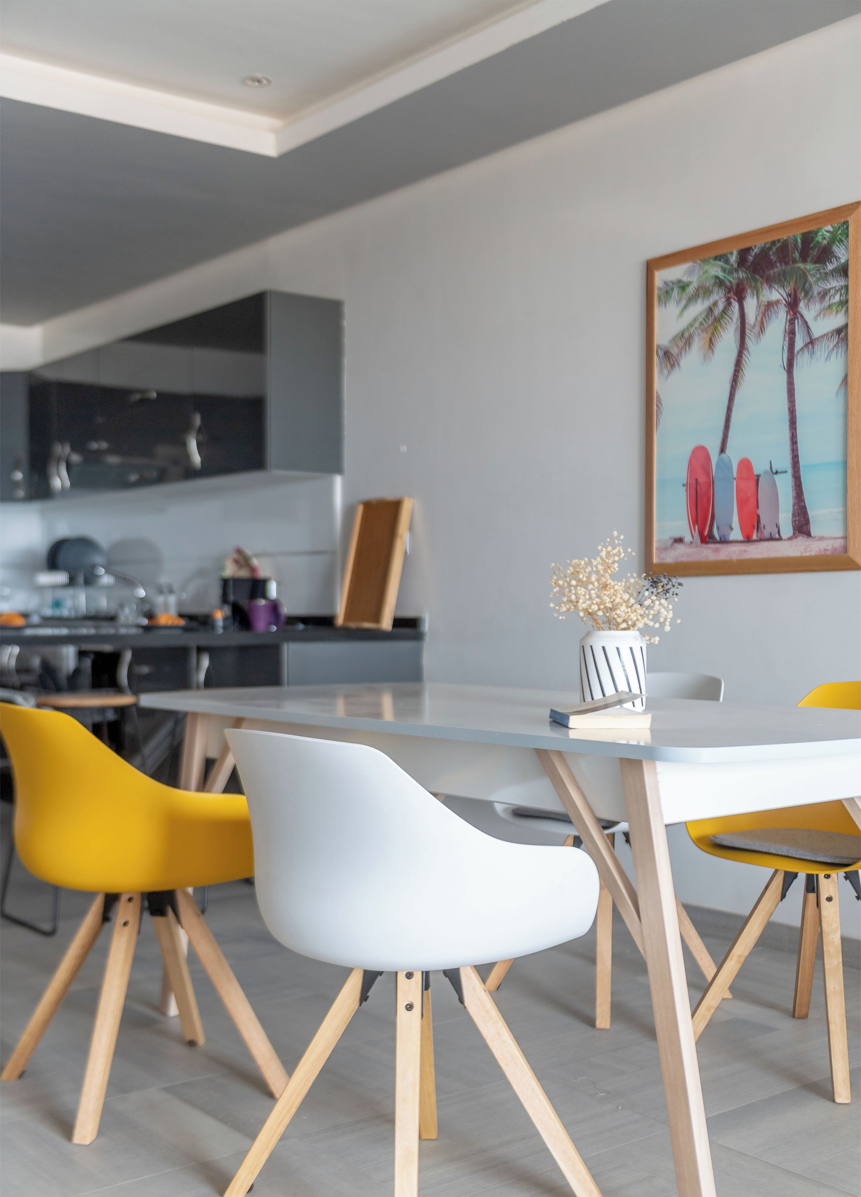 Uma área de refeições moderna com mesa de vidro, cadeiras de madeira e um quadro com pranchas de surf na parede.