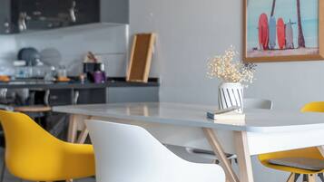 Uma área de refeições moderna com mesa de vidro, cadeiras de madeira e um quadro com pranchas de surf na parede.