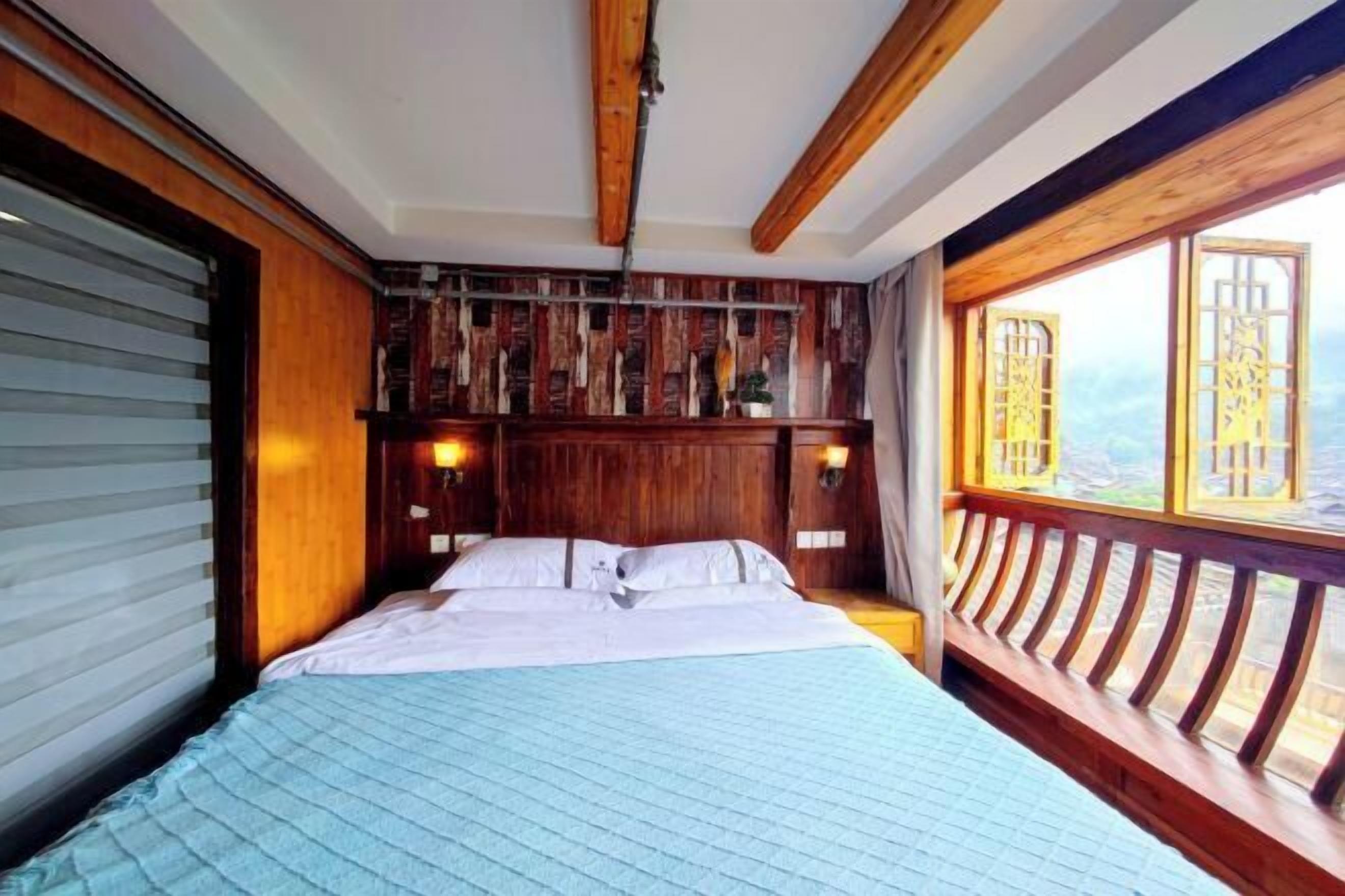 Quarto com cabeceira de madeira, cama com roupa de cama branca e janela com vista para o exterior.