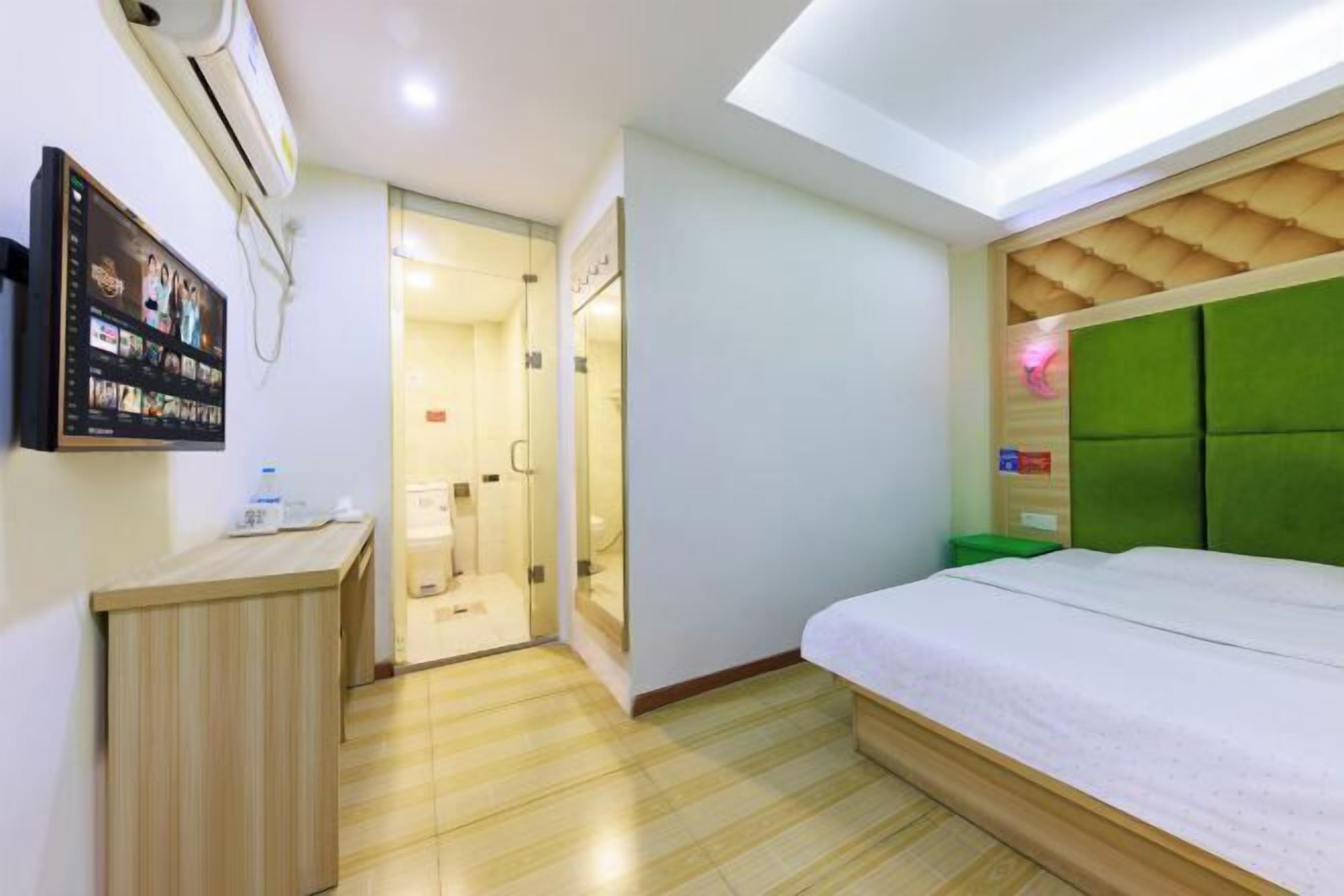 Quarto de hotel com cama, escrivaninha, chuveiro e televisão na parede.