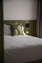 Cama bem arrumada com lençóis brancos e um único travesseiro verde.
