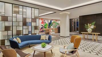 Um lobby moderno com um sofá azul, cadeiras de madeira, uma mesa de centro e uma parede decorativa com arte abstrata.
