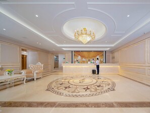 Um hall amplo com um lustre imponente, balcão de recepção e um padrão decorativo no piso.