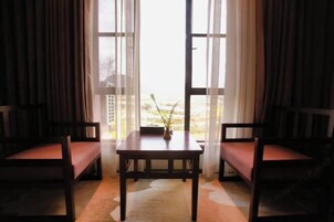 Quarto com duas cadeiras de madeira, uma mesa pequena e vista através de grandes janelas.