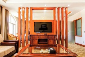 Quarto de hotel com aparador de madeira, televisão de tela plana, mesa de centro de vidro e um sofá.