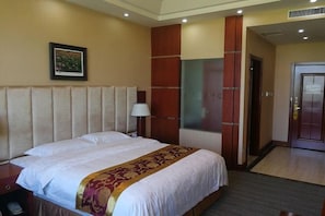 Quarto de hotel com uma cama grande, uma mesa de cabeceira, uma luminária, uma porta e um quadro pendurado na parede.