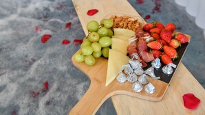 Tábua de madeira com uvas, queijo, morangos e bombons embalados.