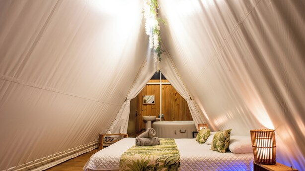 Aconchegante acomodação em tenda com cama, um banco de madeira, luminária pendente e uma pia pequena.