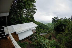 Um deck de madeira com toldo branco, com vista para uma paisagem verdejante, um rio e colinas ao longe.