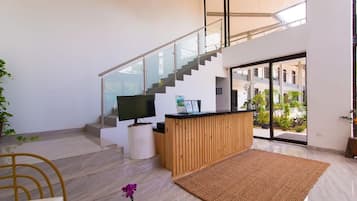 Um interior moderno com balcão de recepção, TV de tela plana, escada e uma grande porta de vidro que dá para uma área externa.